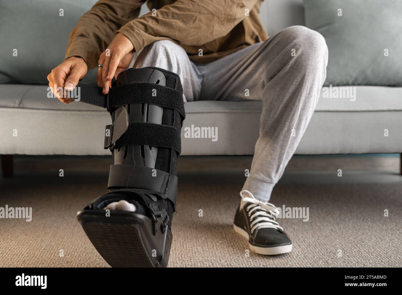 Injury young man putting-up black splint on leg sitting on the sofa ...