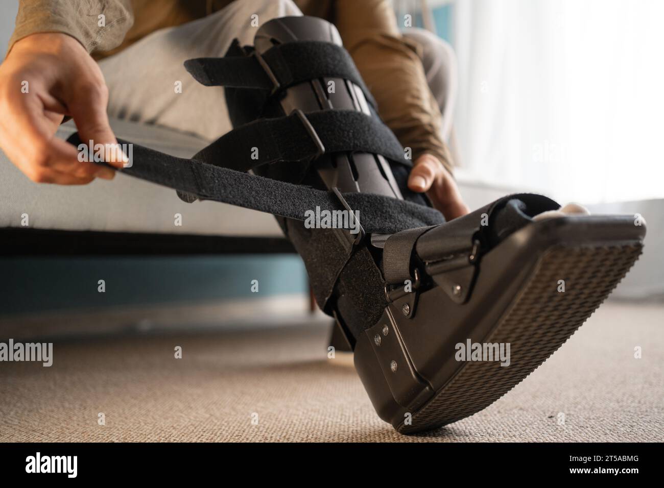 Man take-off ankle orthosis on leg sitting on the sofa at home. Ankle ...