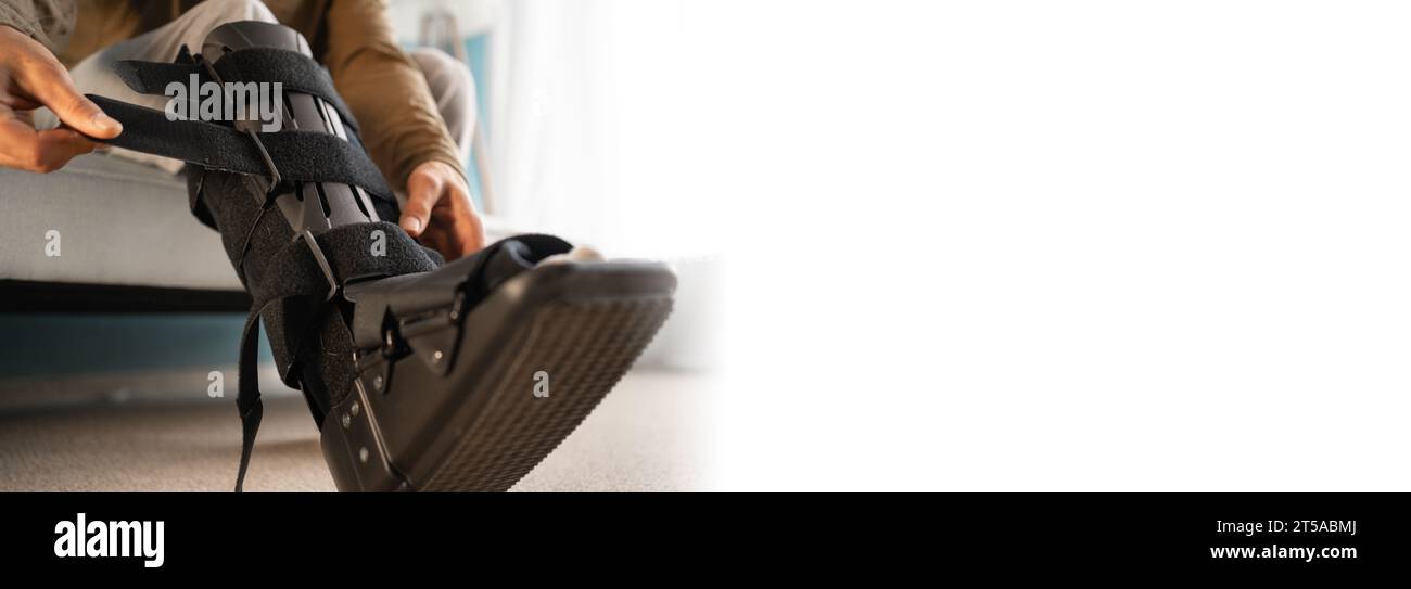Ankle foot orthosis after injury. Man putting ankle orthosis on leg sitting on the sofa at home ...