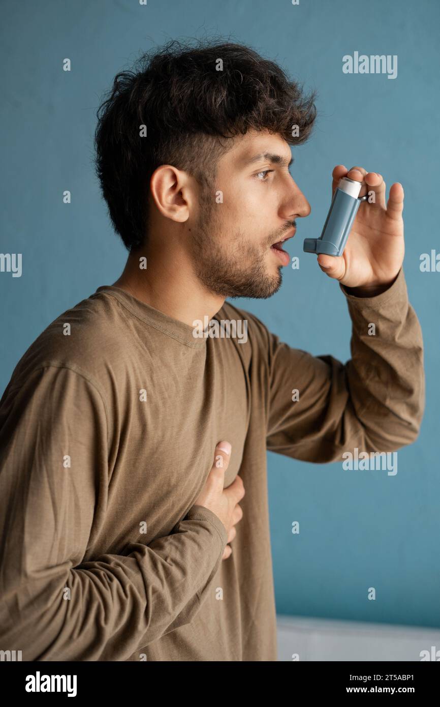 portrait of arabic young man using asthma inhaler against blue ...