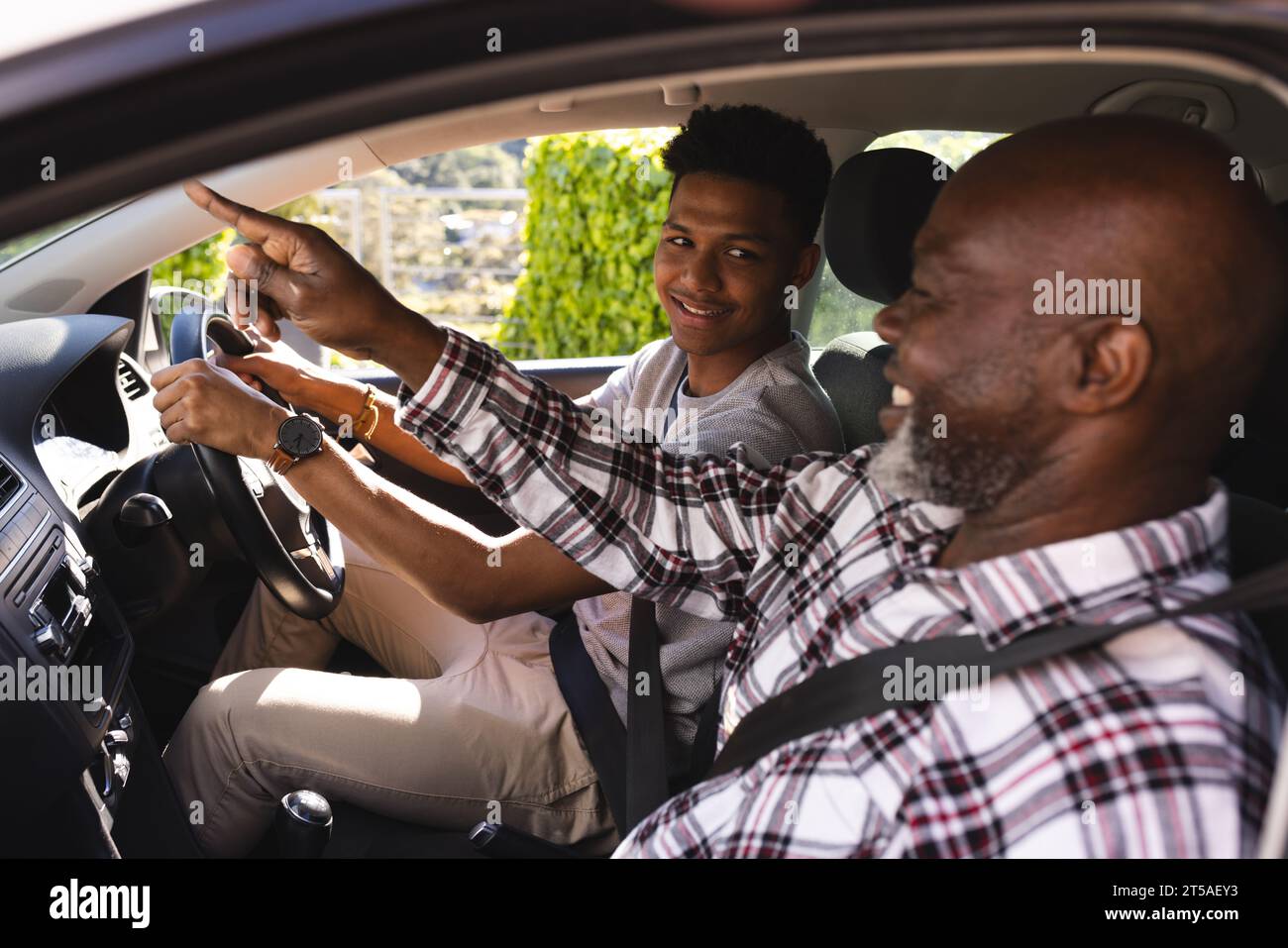Happy african american father teaching and adult son in car during ...
