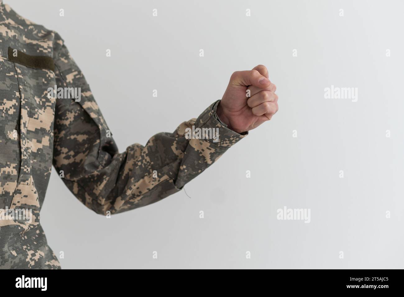 Hand in camouflage shows gesture on gray background. Fingers clenched ...