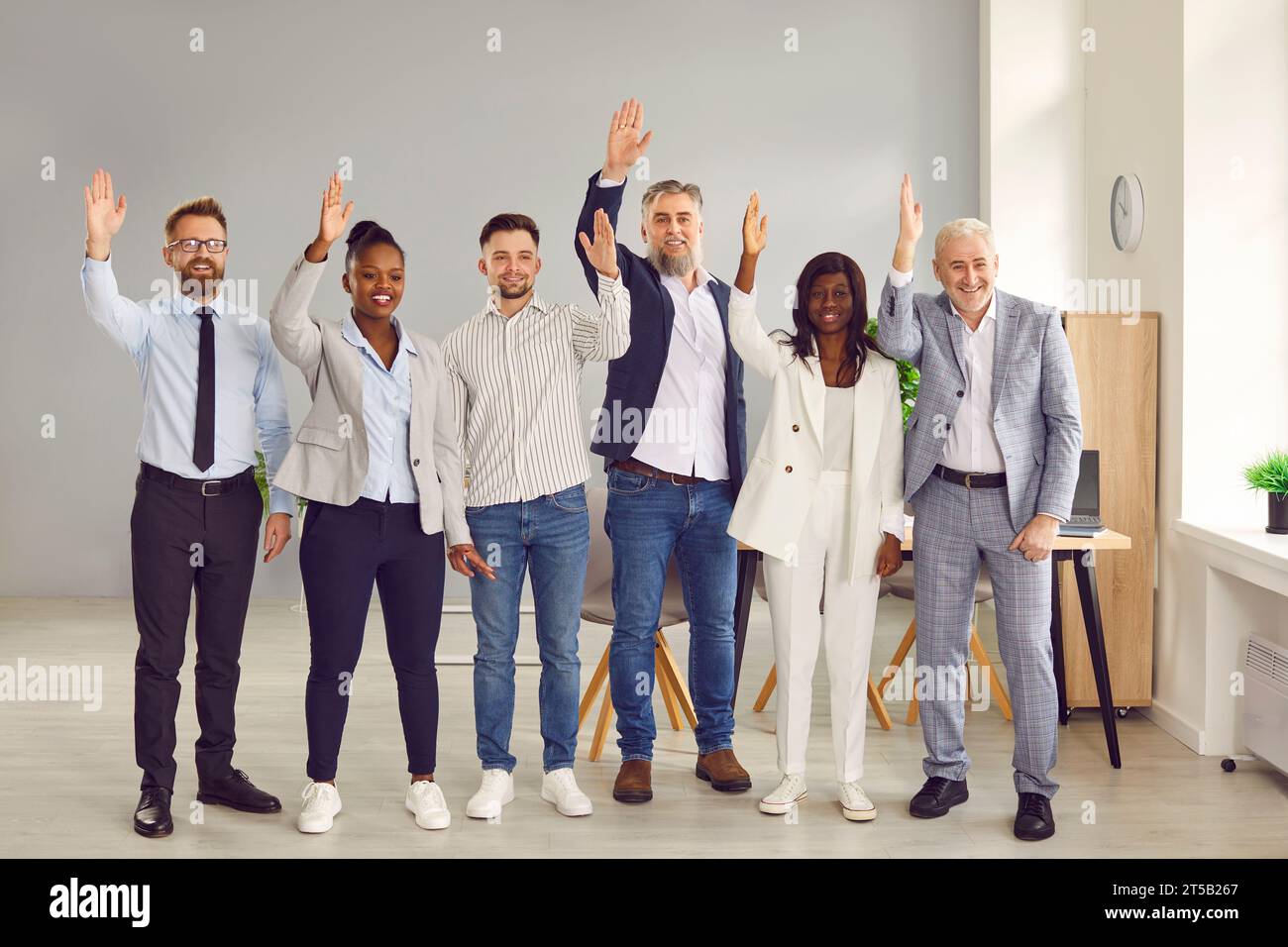 Portrait of employees standing in a row in office and raising their ...