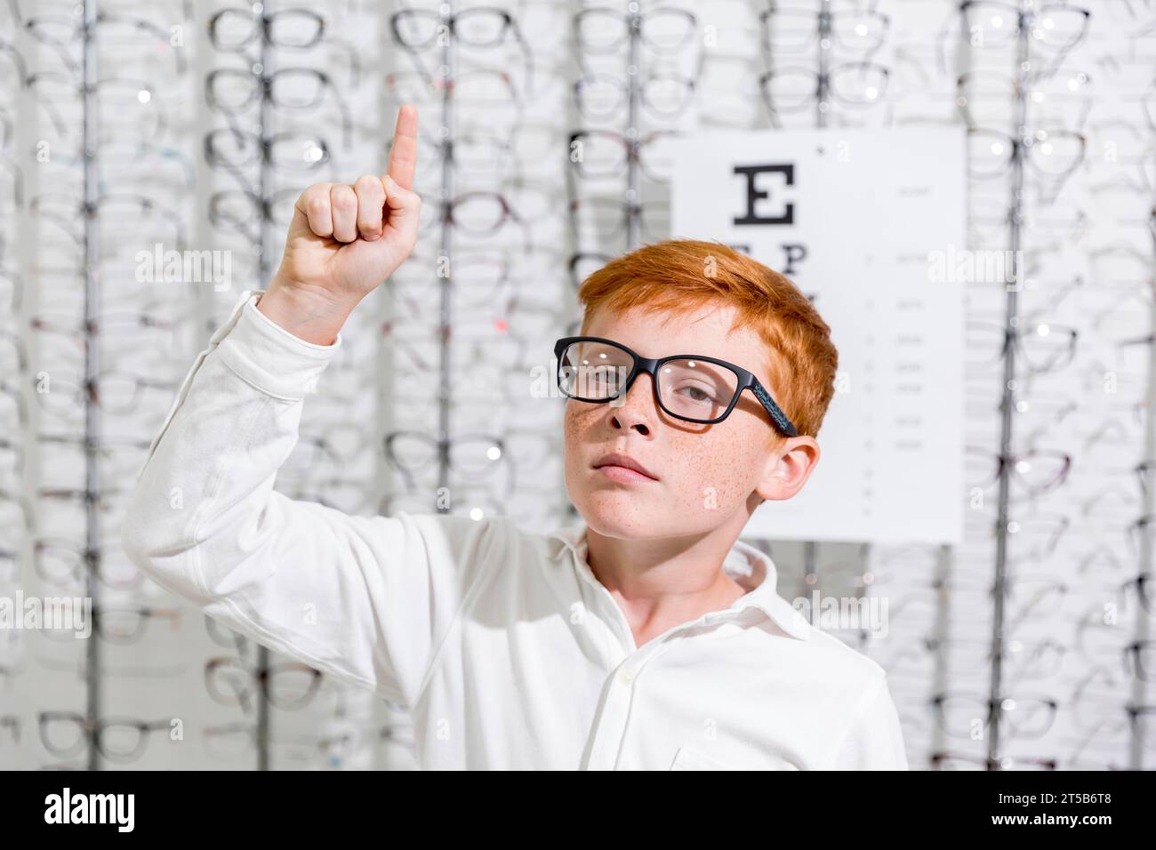 Boy with spectacle pointing upward direction standing against ...