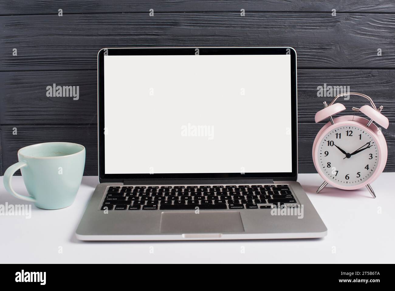 Ceramics cup alarm clock open laptop white desk against wooden black ...