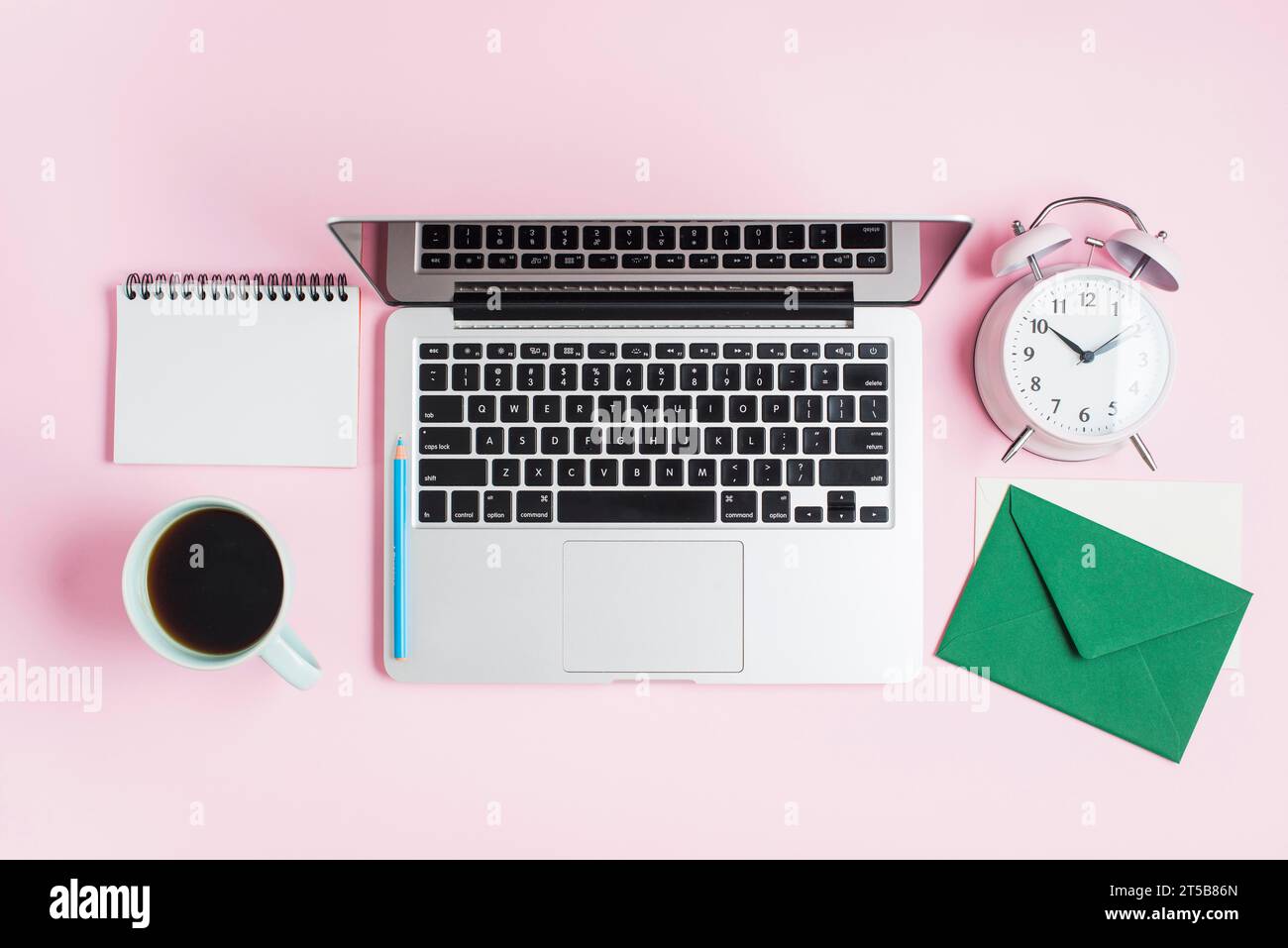 Open laptop pencil alarm clock spiral notepad envelope pink background ...