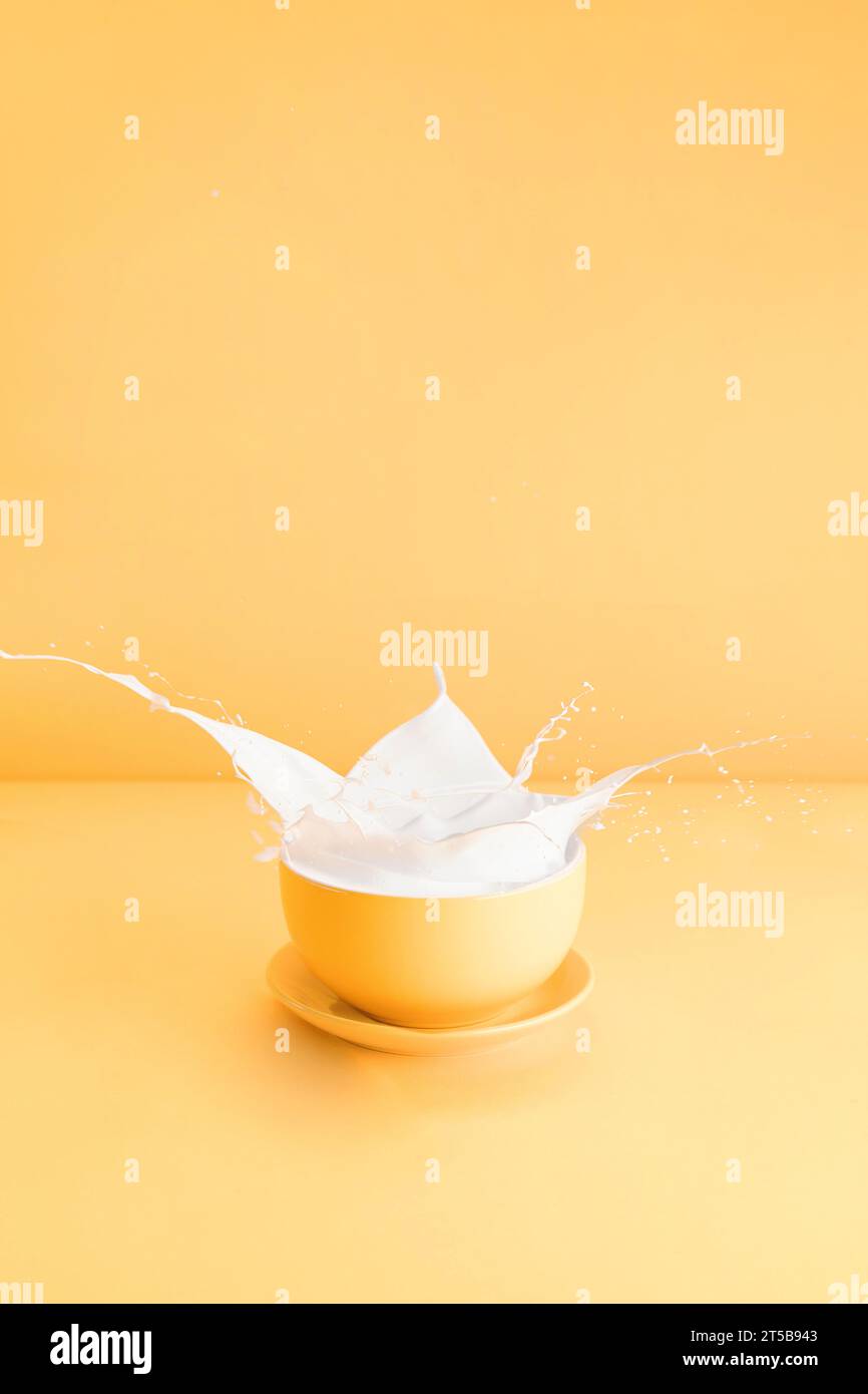 Yellow cup with spilling milk Stock Photo - Alamy