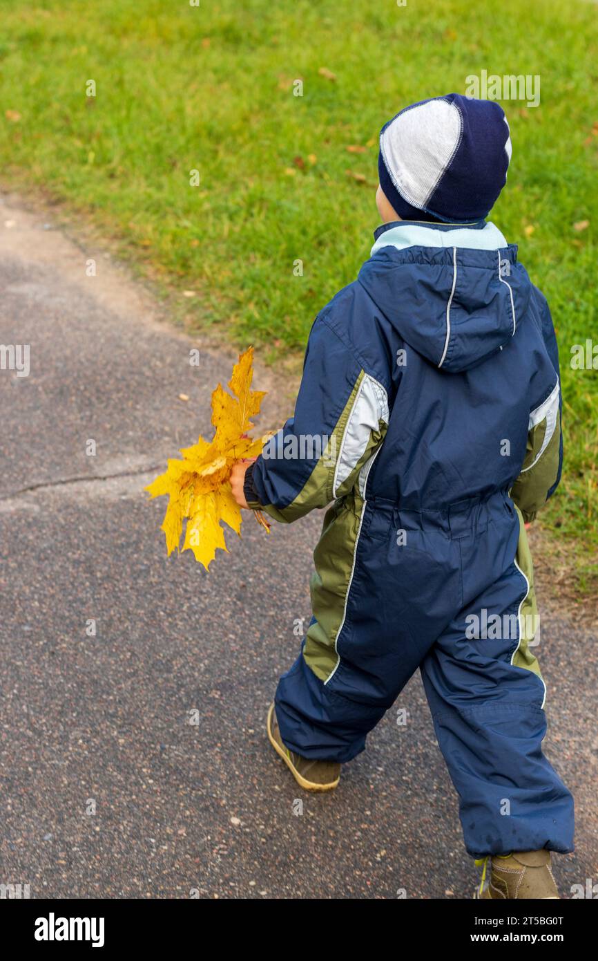 Shot of the little kid, wearing overalls, Walking in the park, carrying ...