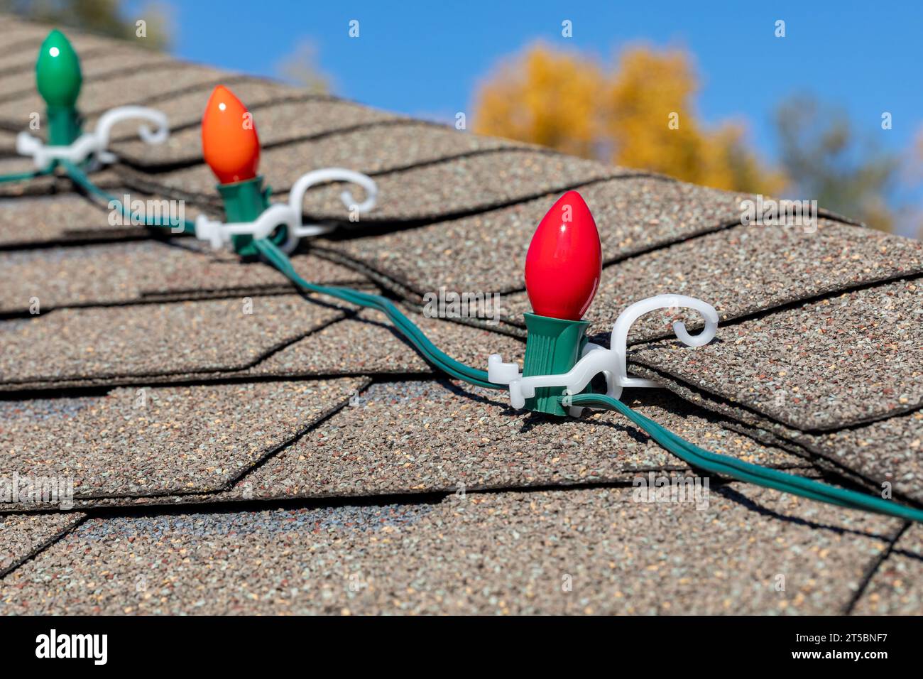 Hanging Christmas string lights on shingles of roof. Holiday decorating ...