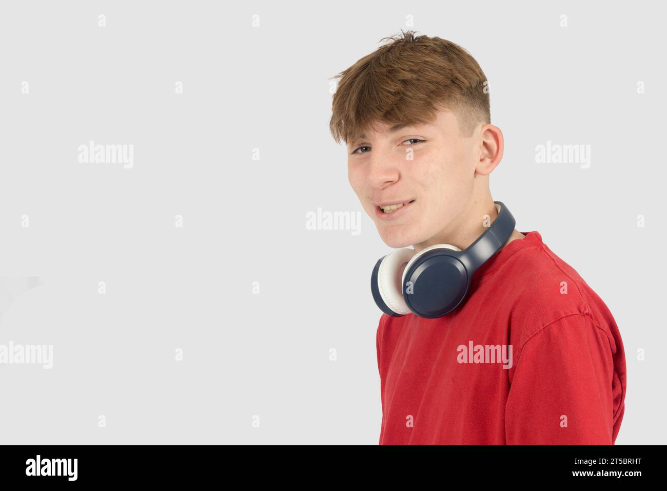Caucasian 15 year old teenage boy, wearing a red t-shirt, with headphones loose around his neck ...