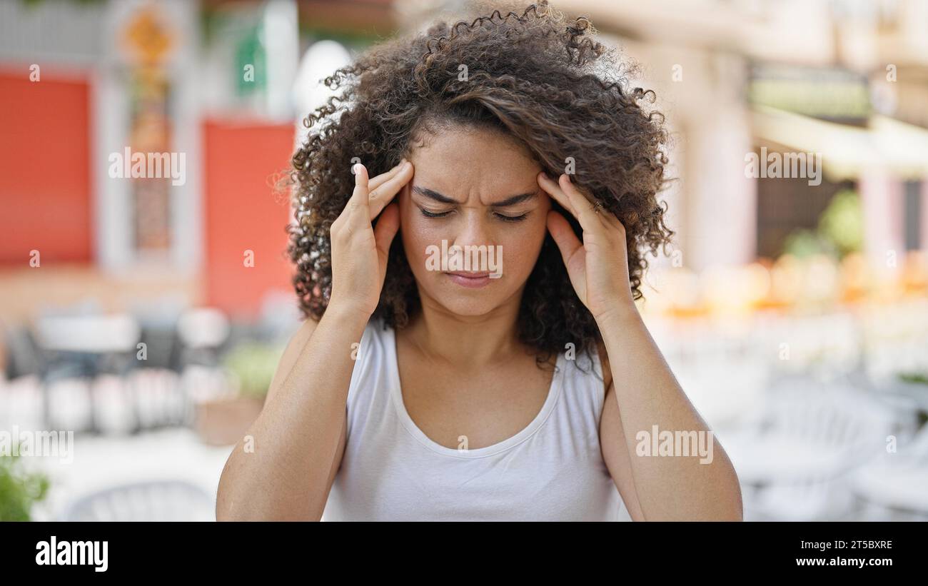 Young beautiful hispanic woman suffering for headache at coffee shop ...