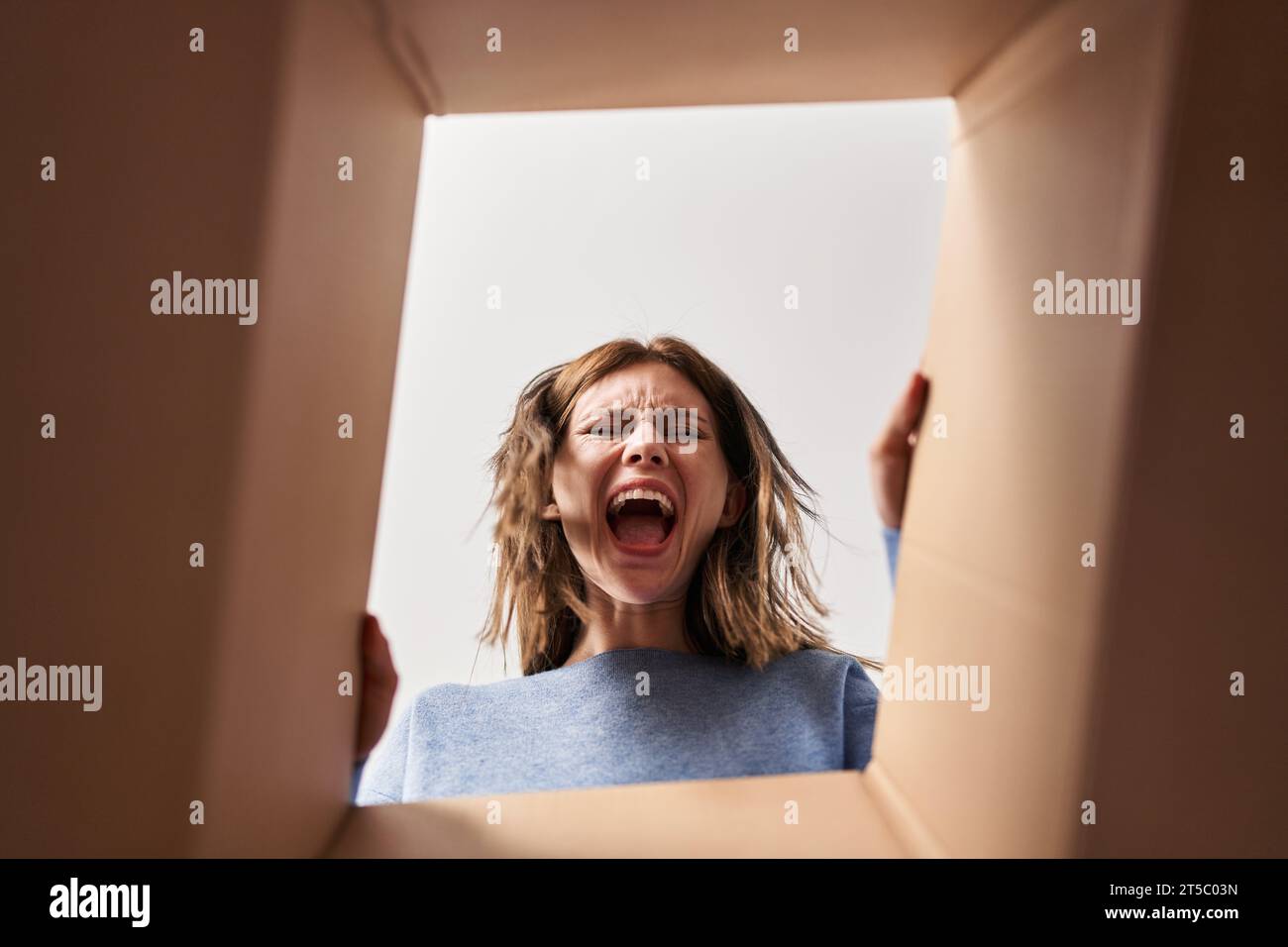 Beautiful woman opening cardboard box angry and mad screaming ...
