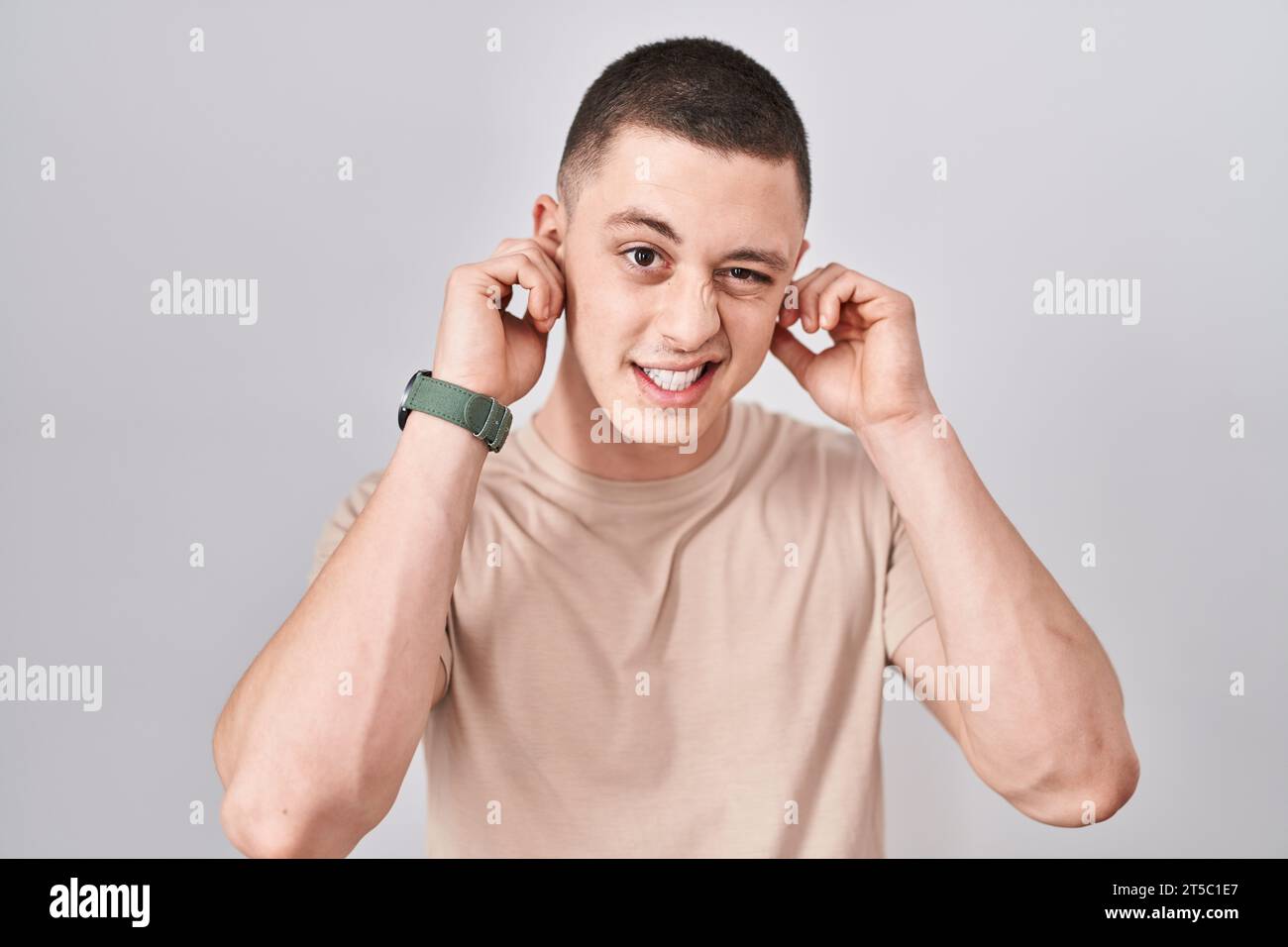 Young man standing over isolated background covering ears with fingers ...
