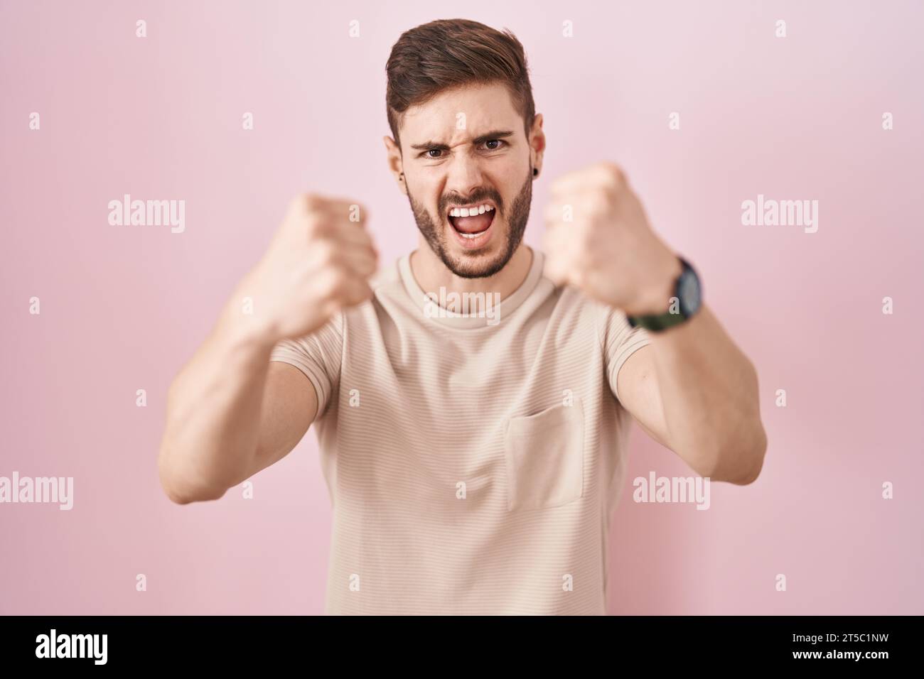 Hispanic man with beard standing over pink background angry and mad ...