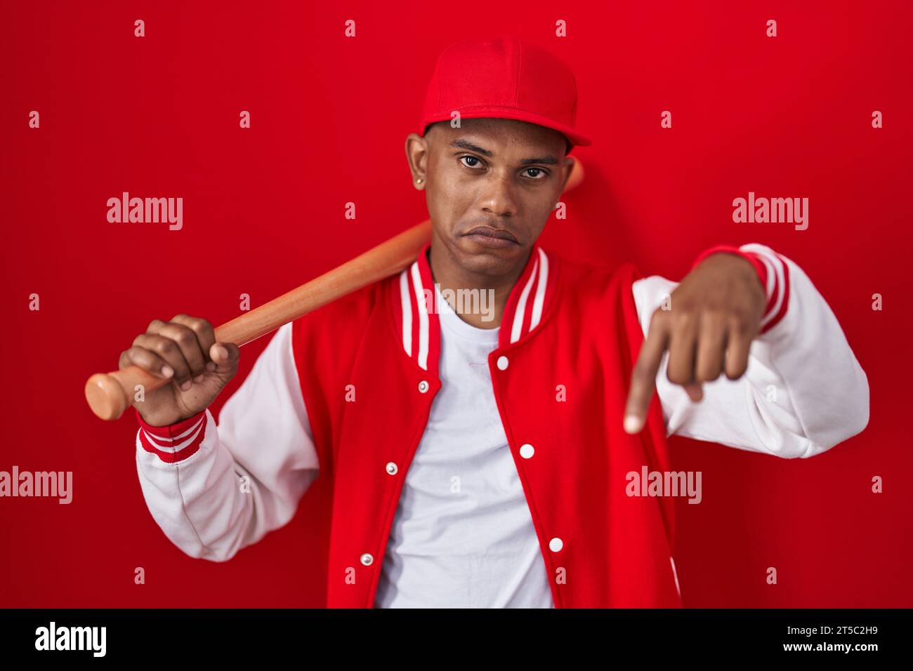Young hispanic man playing baseball holding bat pointing down looking ...