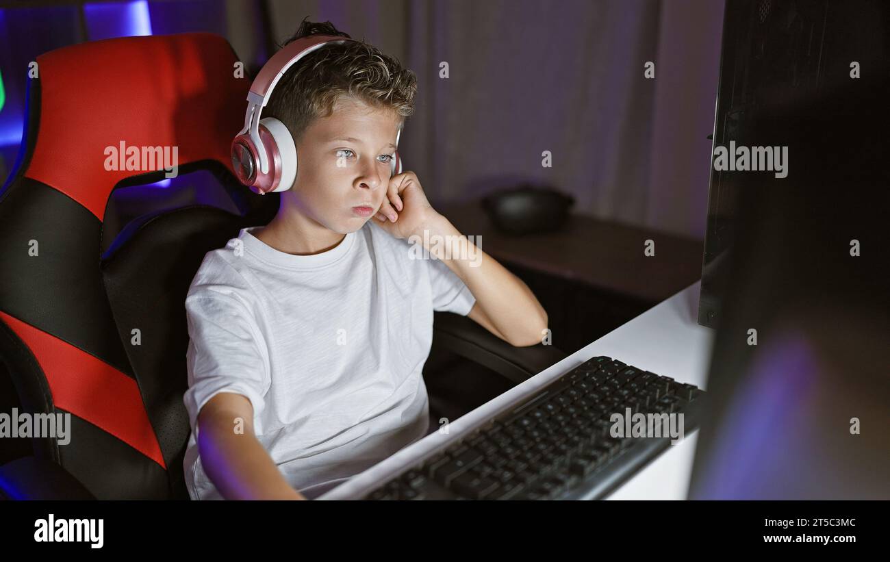 Adorable blond boy streamer, engrossed playing a futuristic video game ...