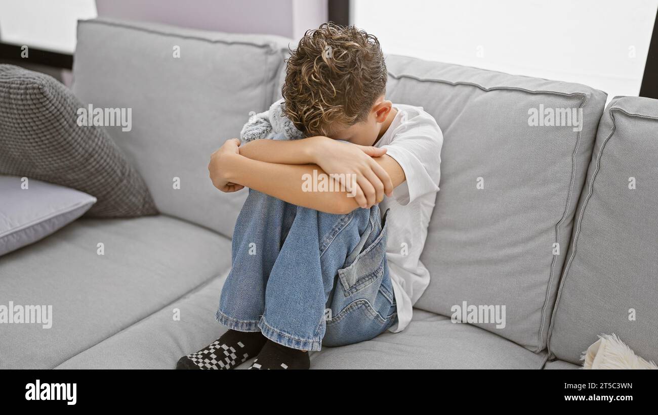 Adorable blond kid hugging teddy bear, crying alone on sofa, expressing ...