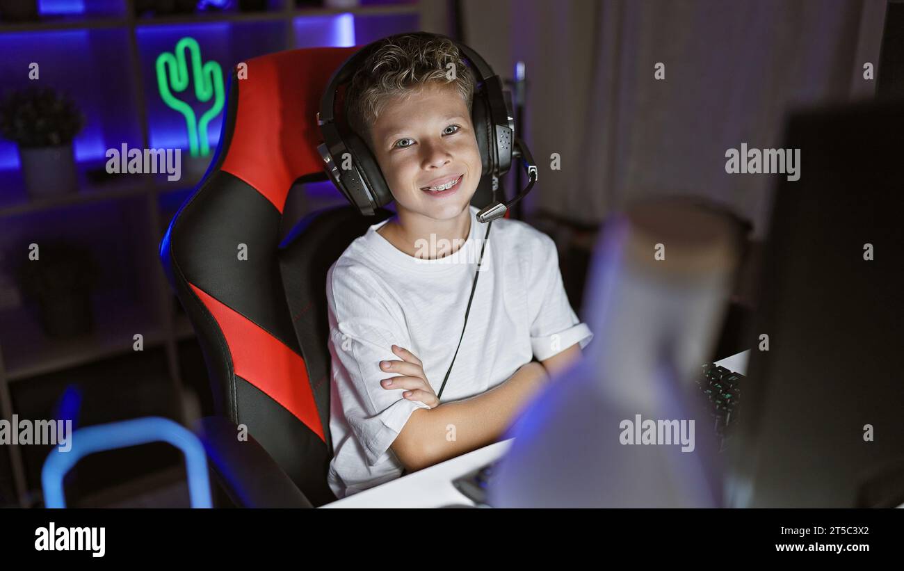 Cute blond boy streamer, engrossed in a digital game, sitting cross ...