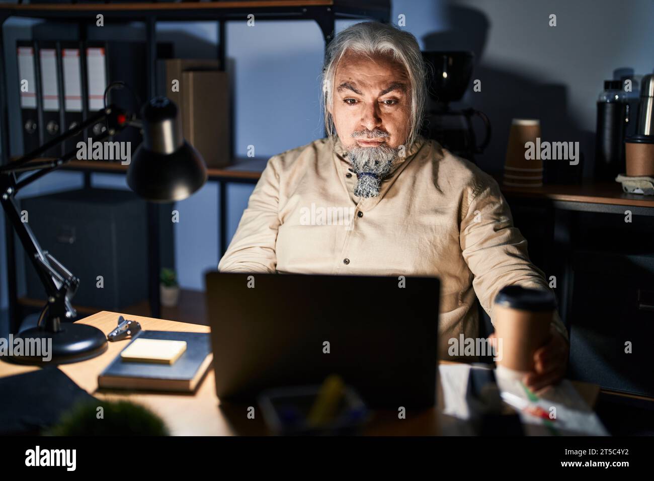 Middle age man with grey hair working at the office at night depressed ...