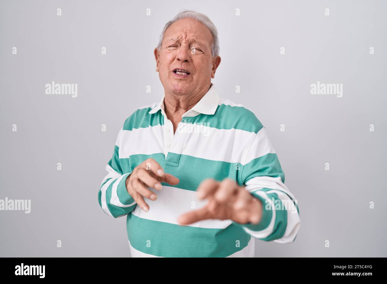 Senior man with grey hair standing over white background disgusted ...