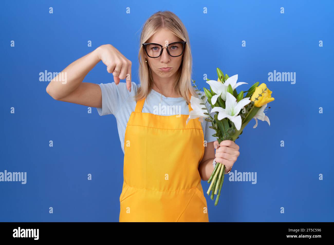 Young caucasian woman wearing florist apron holding flowers pointing ...