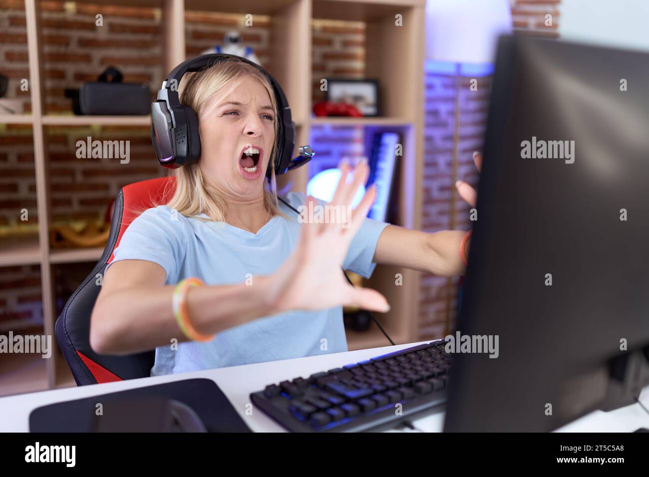 Young caucasian woman playing video games wearing headphones afraid and ...