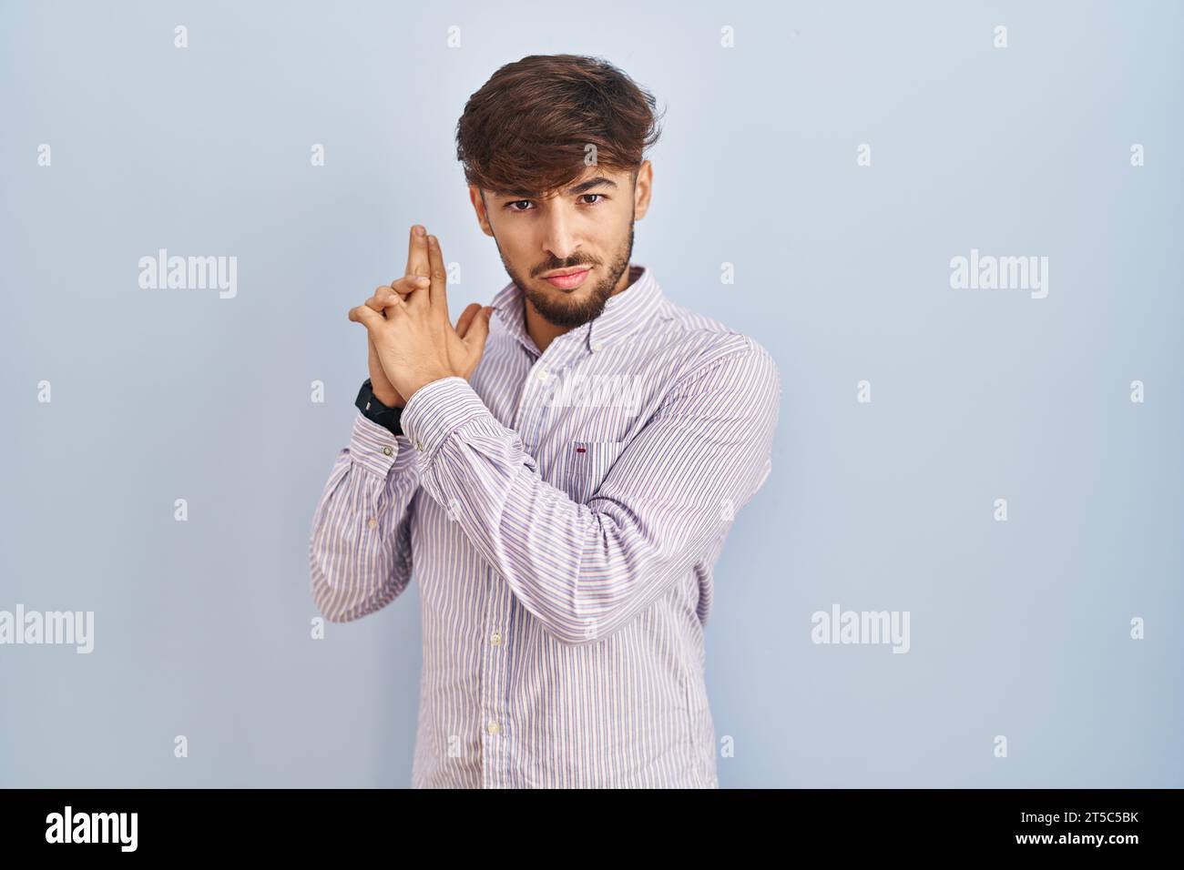 Arab man with beard standing over blue background holding symbolic gun ...