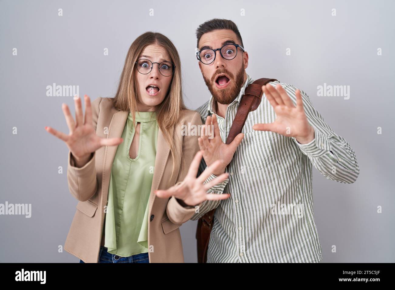 Young couple standing over white background afraid and terrified with ...