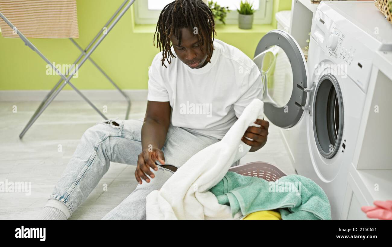 African american man washing clothes sitting on floor at laundry room ...