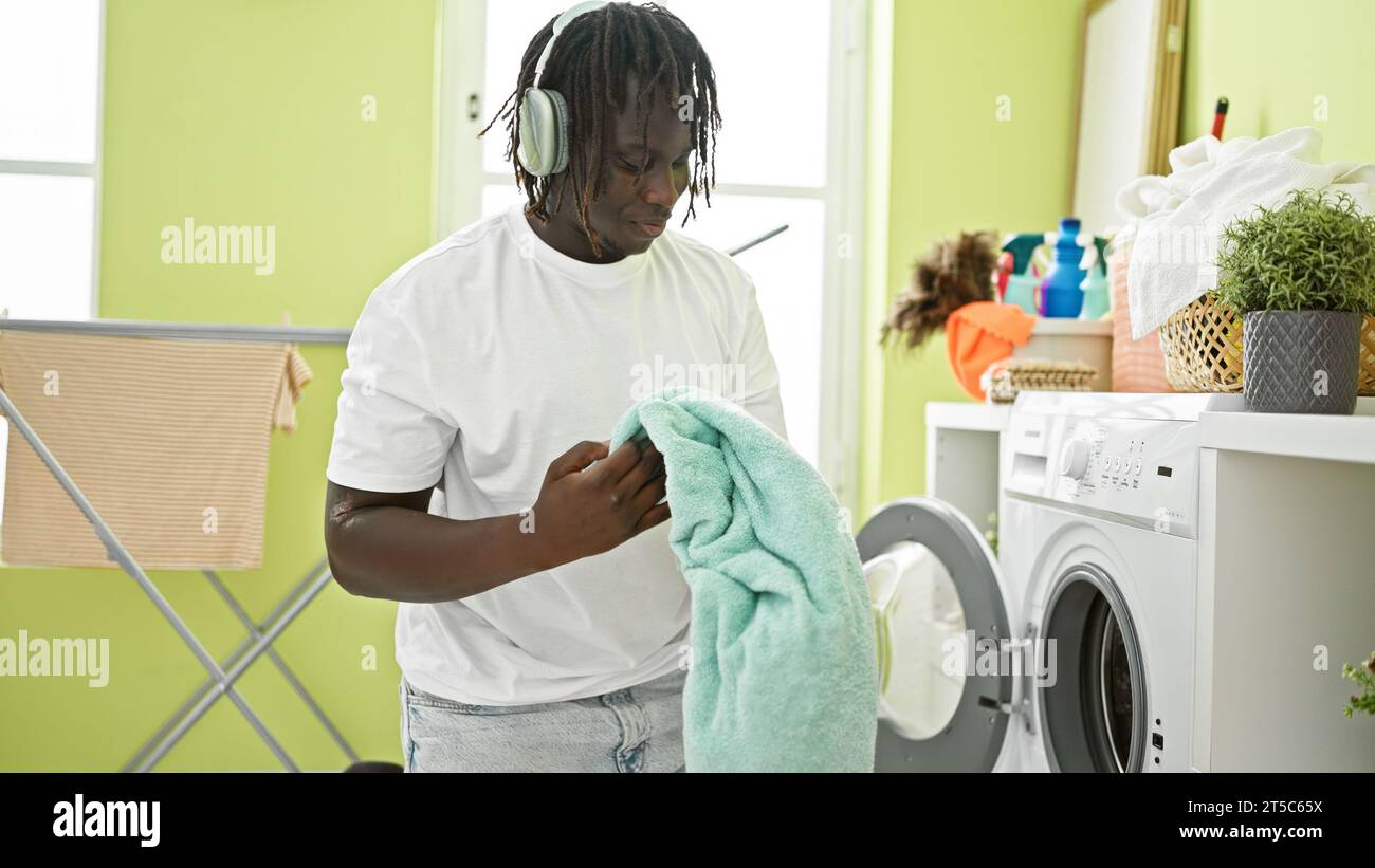 African american man listening to music washing clothes at laundry room ...