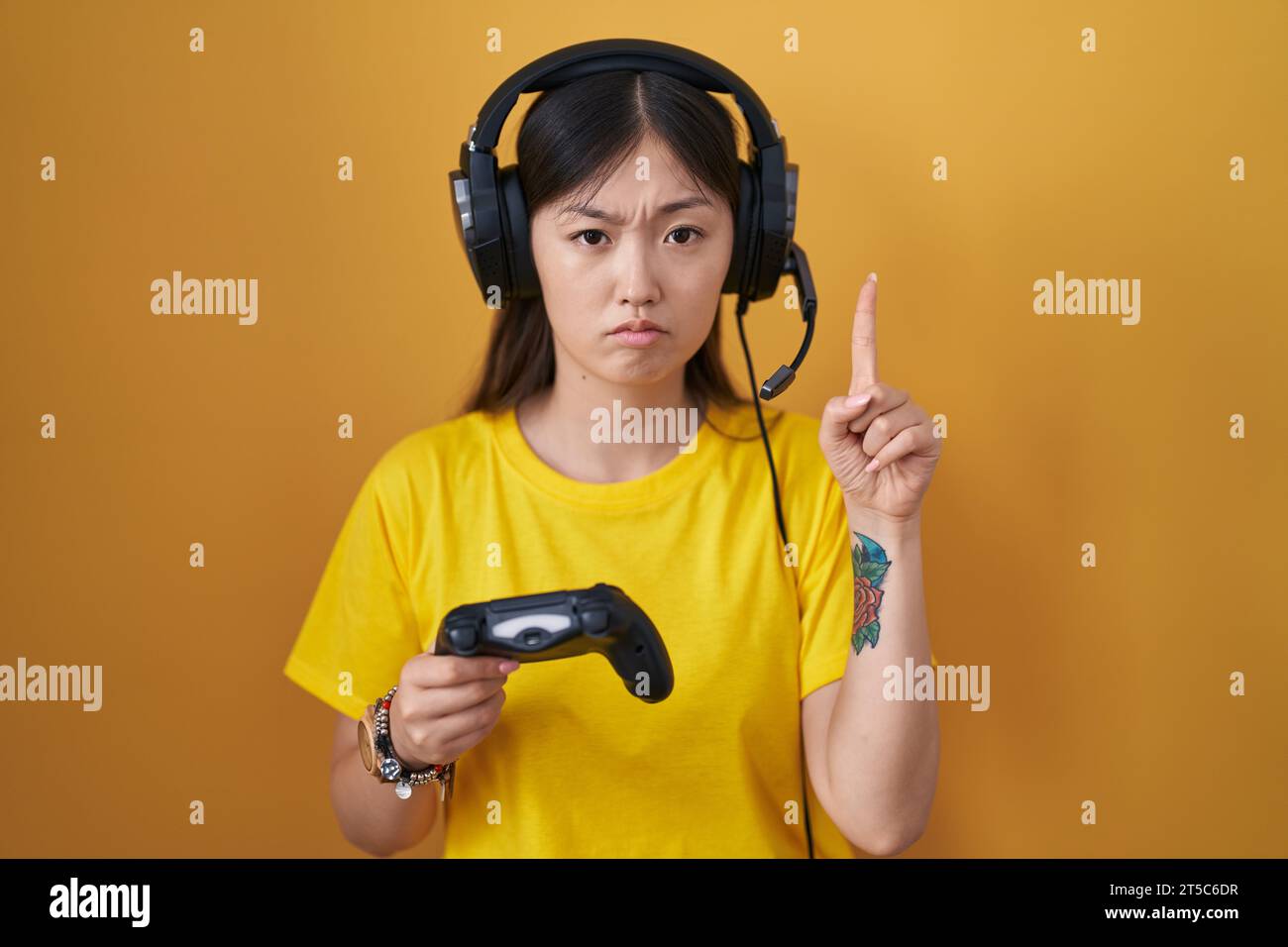 Chinese young woman playing video game holding controller pointing up ...