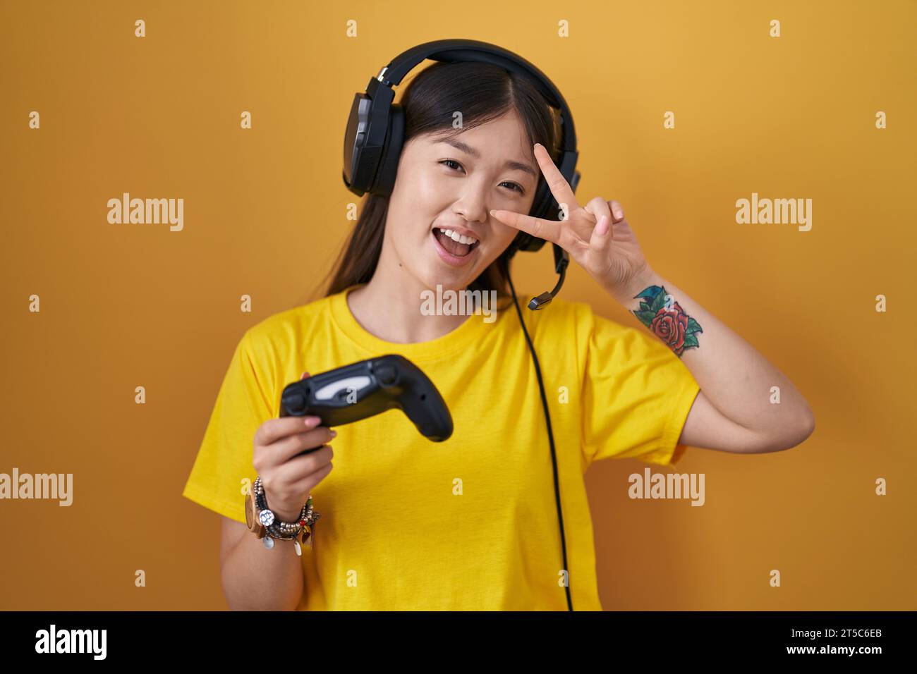 Chinese young woman playing video game holding controller doing peace ...