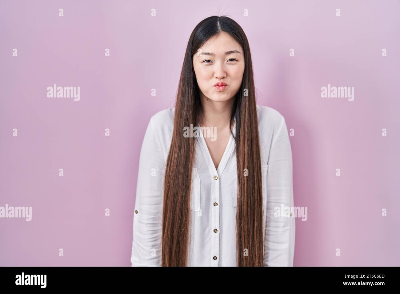 Chinese young woman standing over pink background puffing cheeks with ...