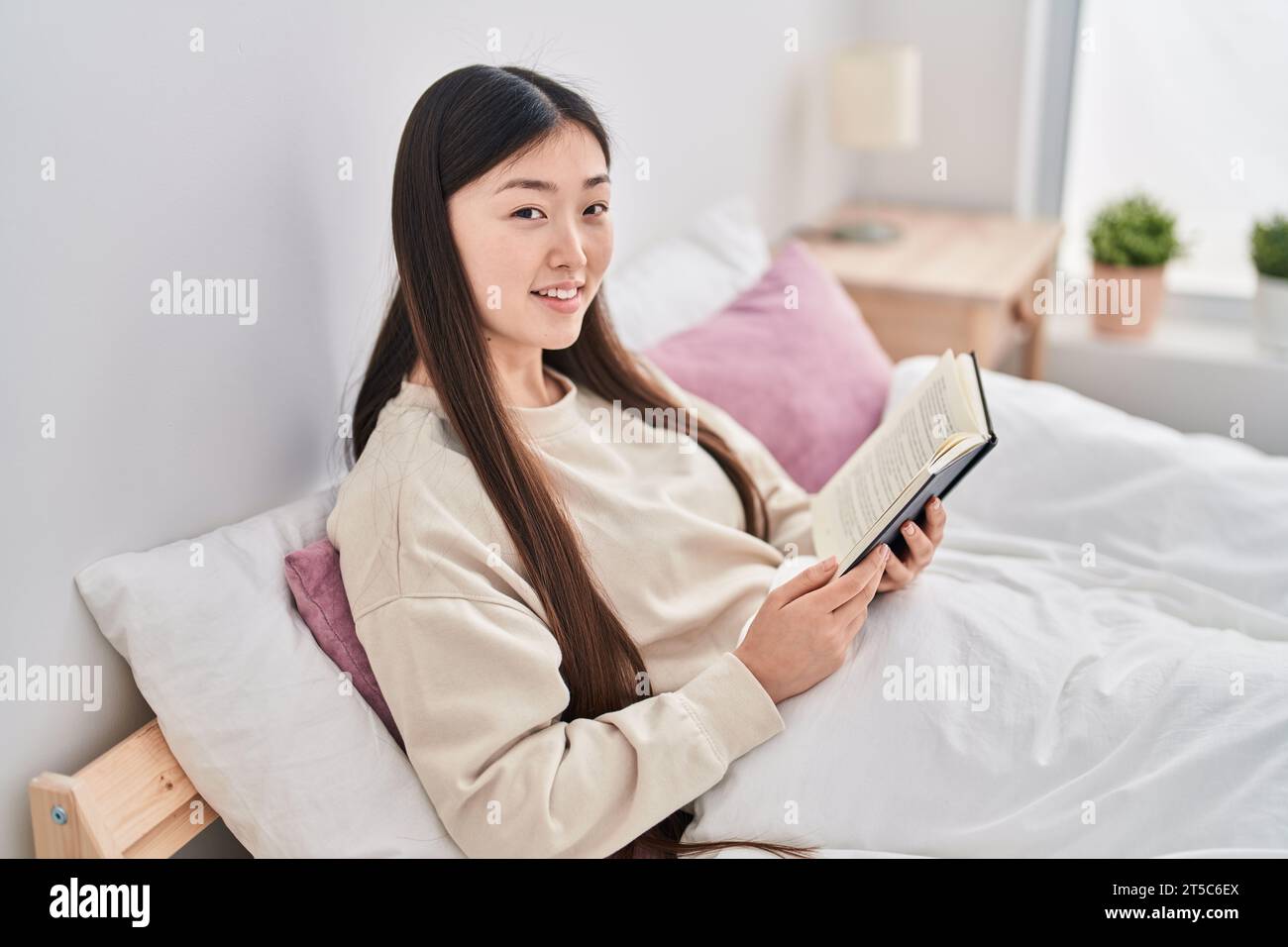 Chinese woman reading book sitting on bed at bedroom Stock Photo - Alamy