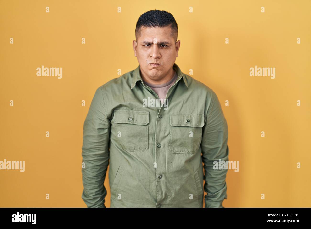 Hispanic young man standing over yellow background skeptic and nervous ...