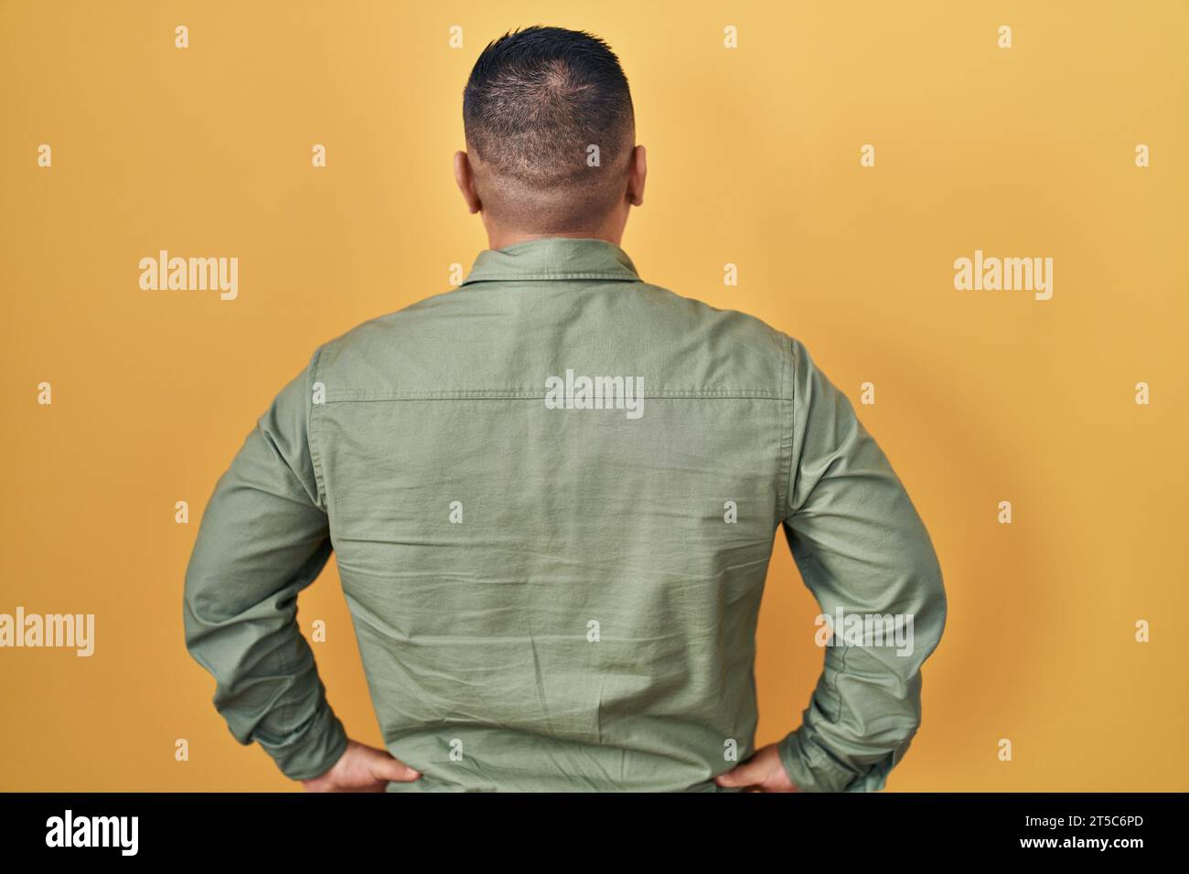 Hispanic young man standing over yellow background standing backwards ...