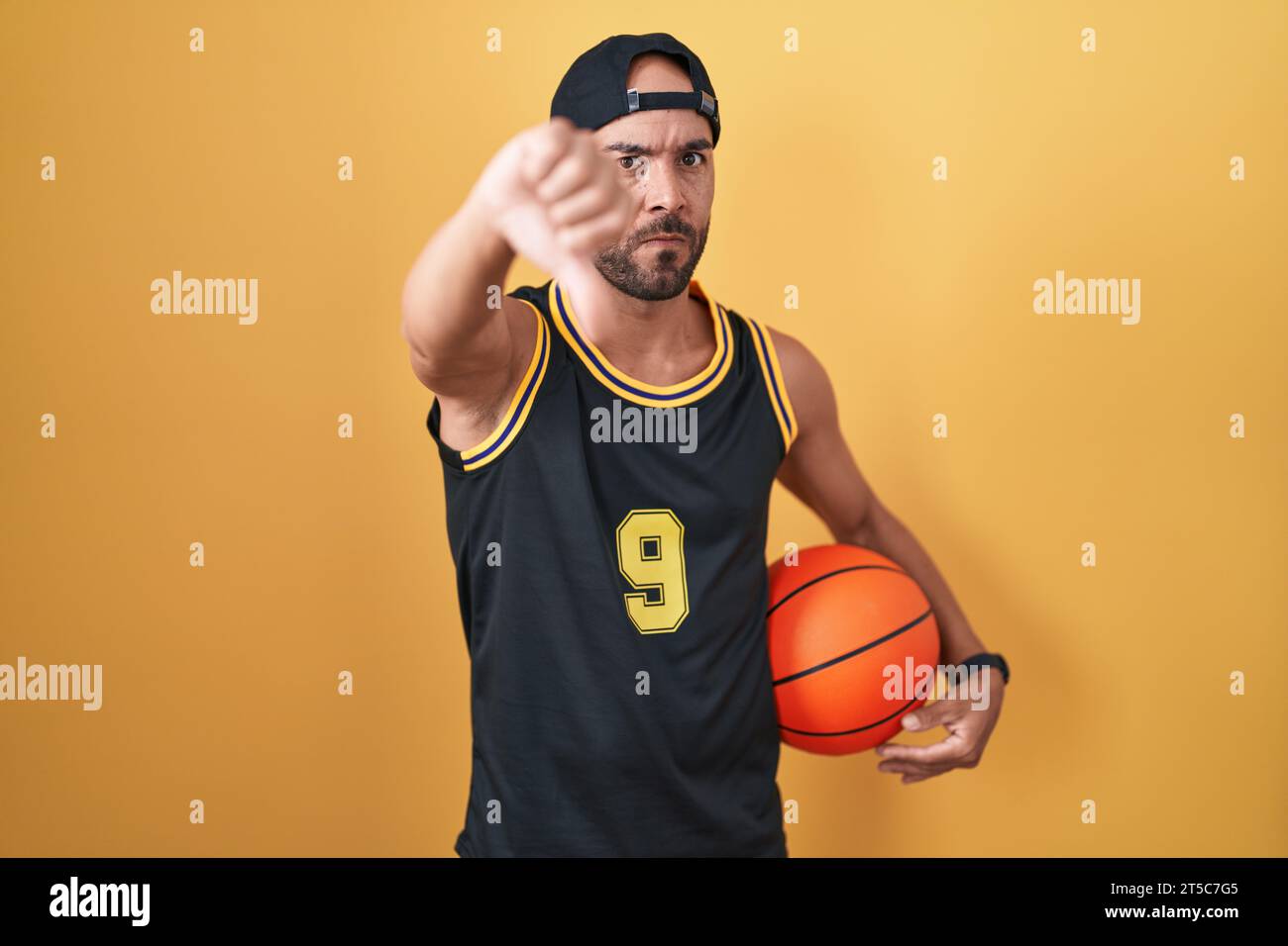 Middle age bald man holding basketball ball over yellow background ...