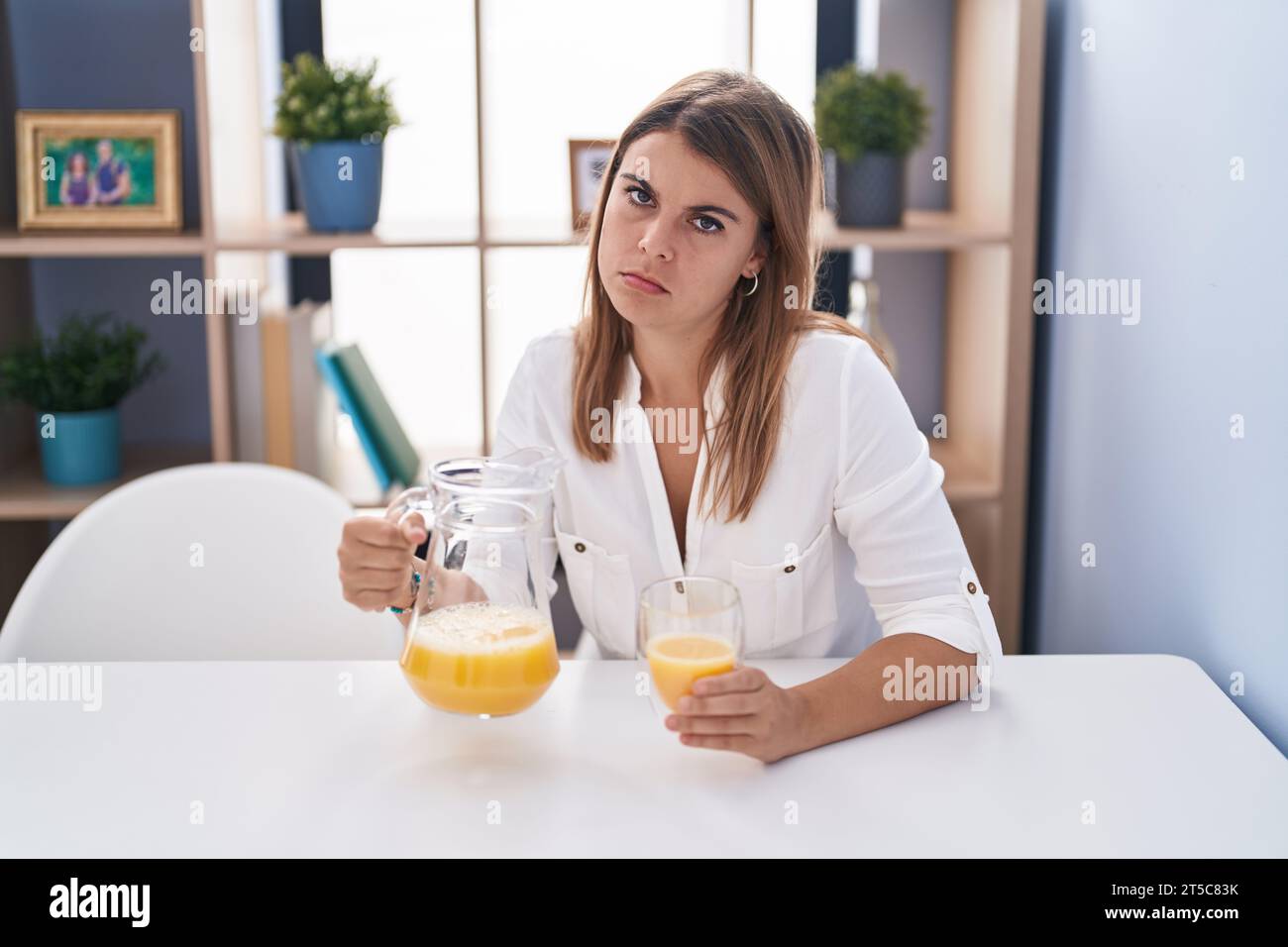 Young hispanic woman drinking glass of orange juice depressed and worry ...
