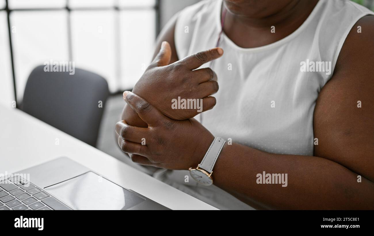 Overworked african american businesswoman grips her aching wrist ...