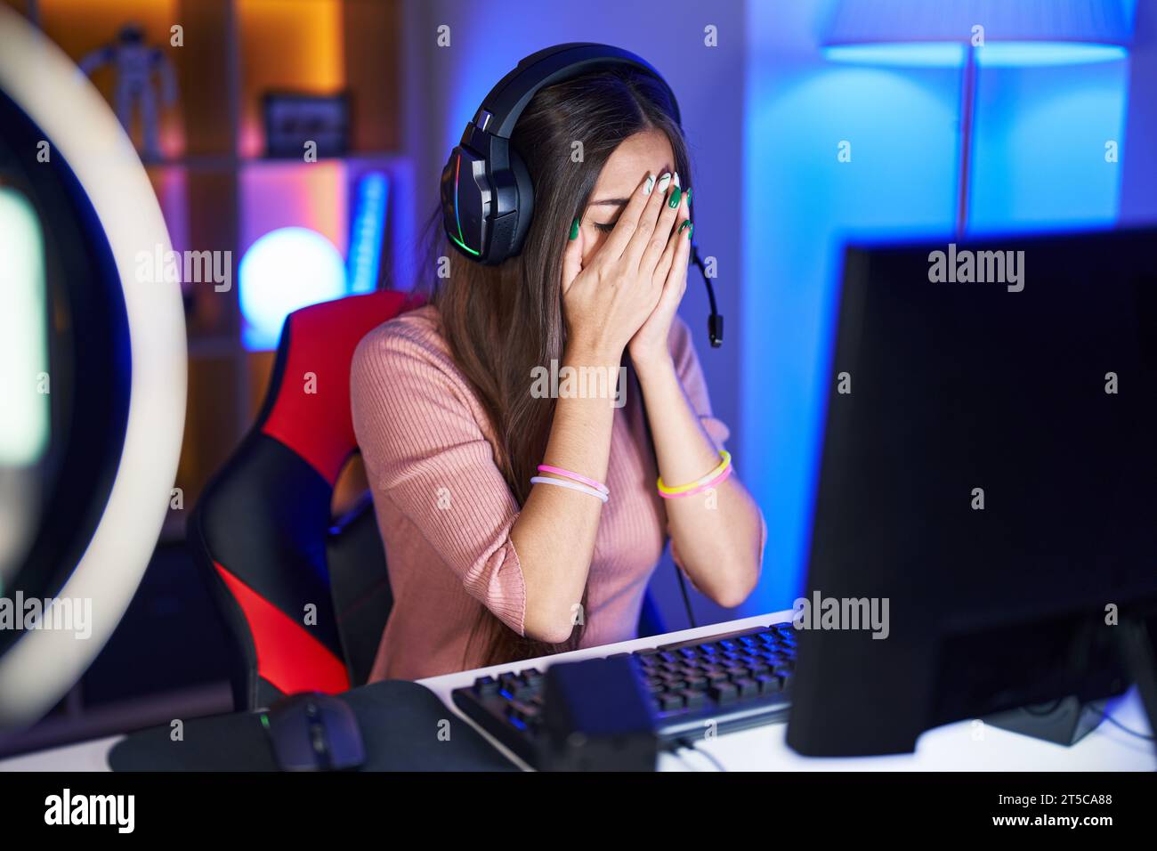 Young hispanic woman playing video games with sad expression covering ...