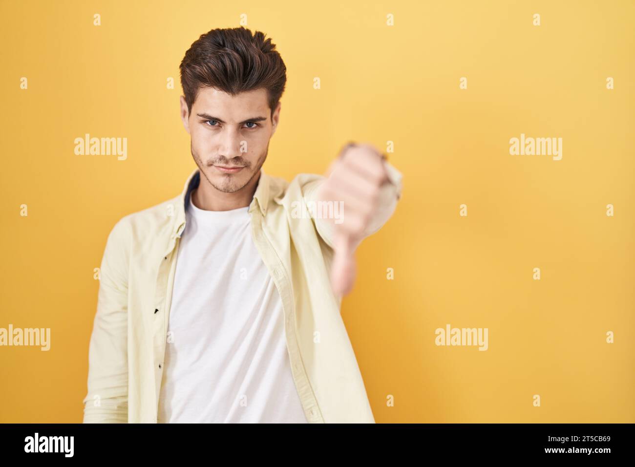 Young hispanic man standing over yellow background looking unhappy and ...
