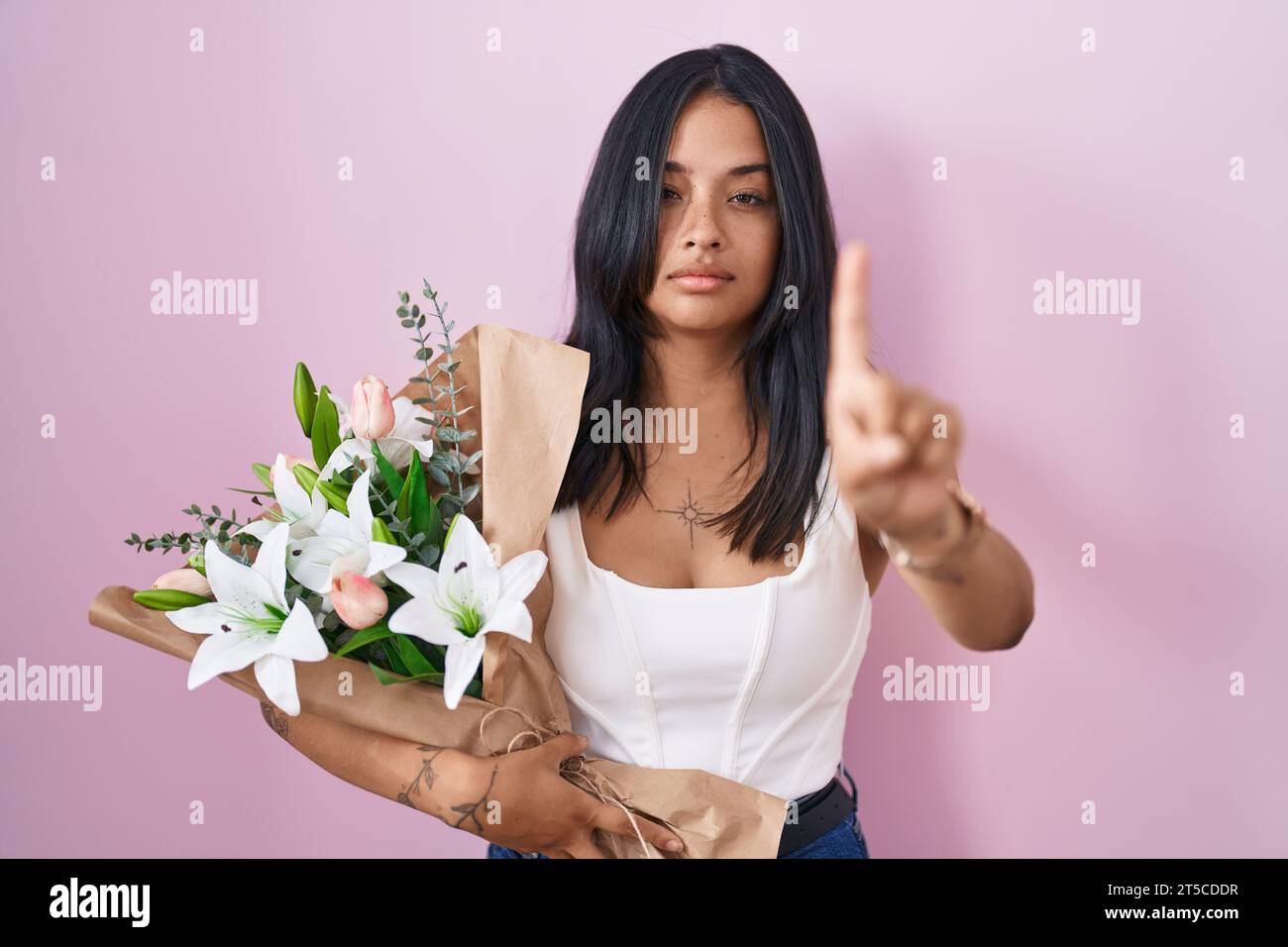 Brunette woman holding bouquet of white flowers pointing with finger up ...