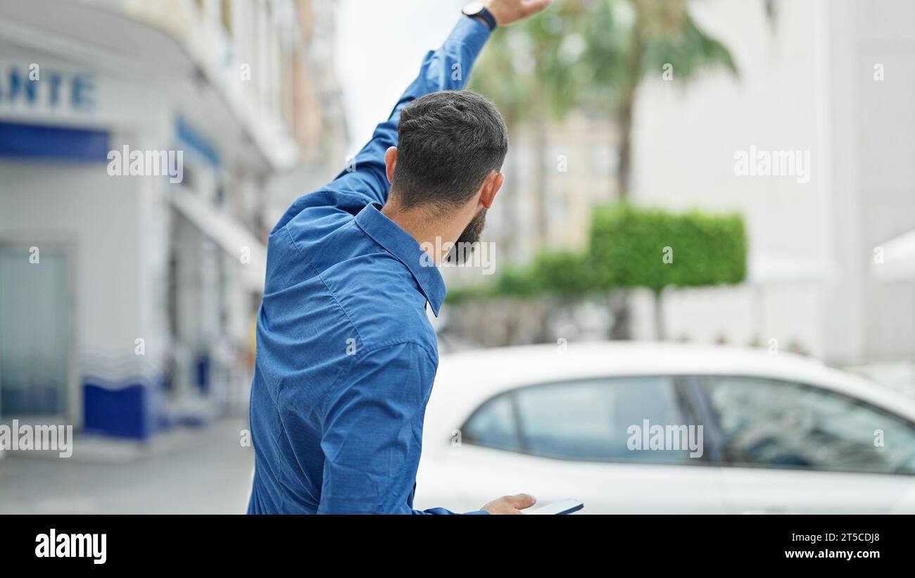Young hispanic man stopping taxi with hand raised up using smartphone ...