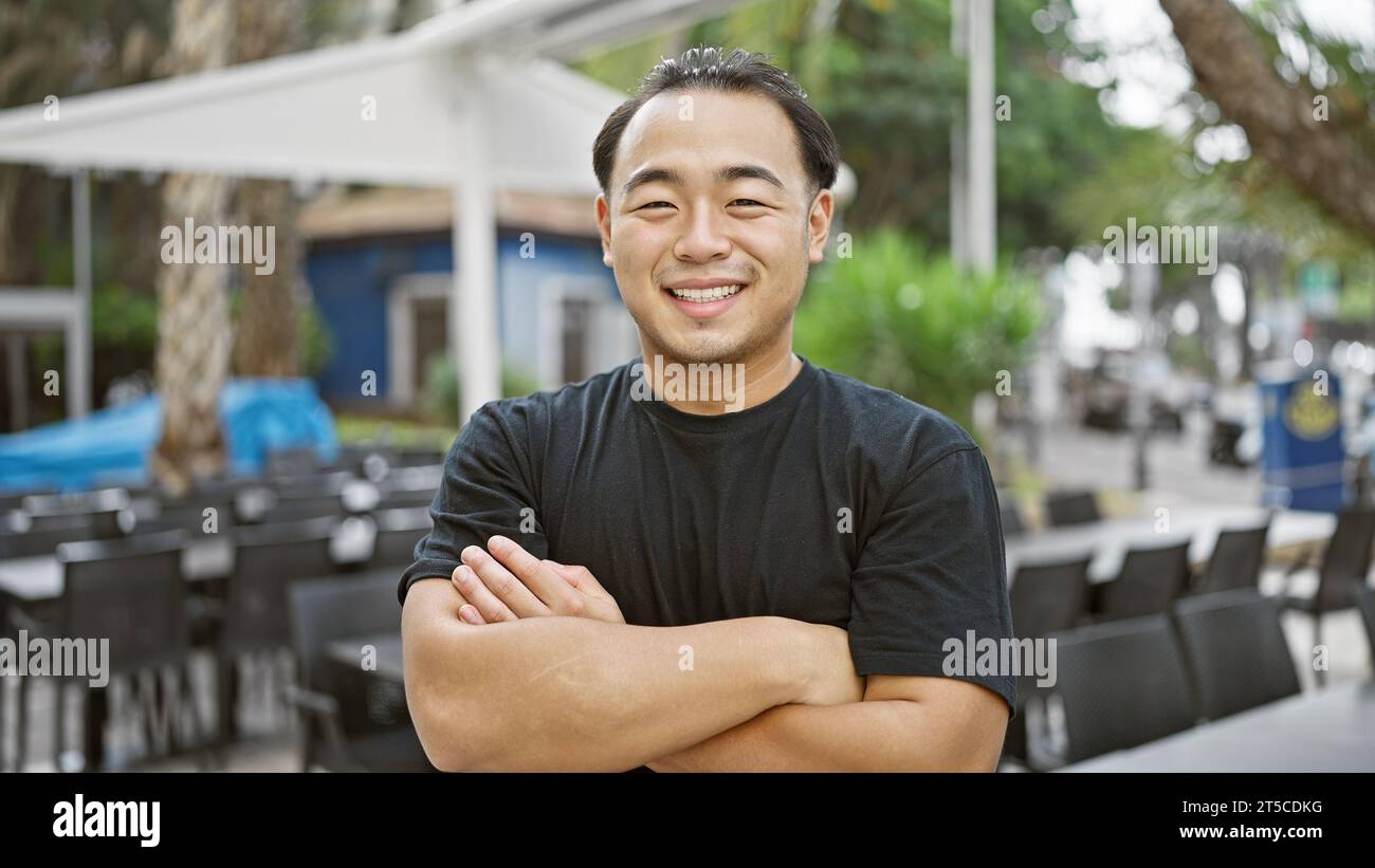Cheerful young chinese man, arms crossed, confidently standing on ...