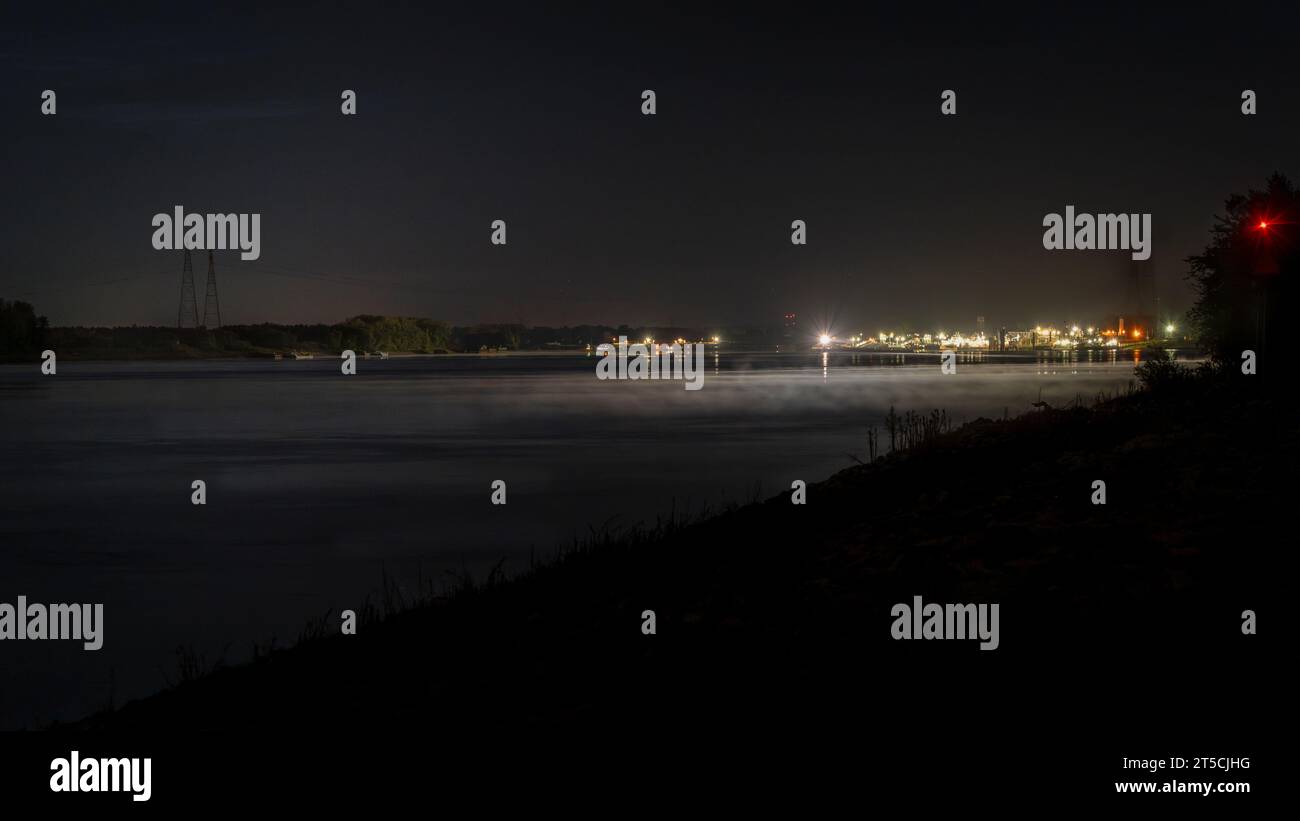 night on the Mississippi River with lights of shipyard facilities above ...