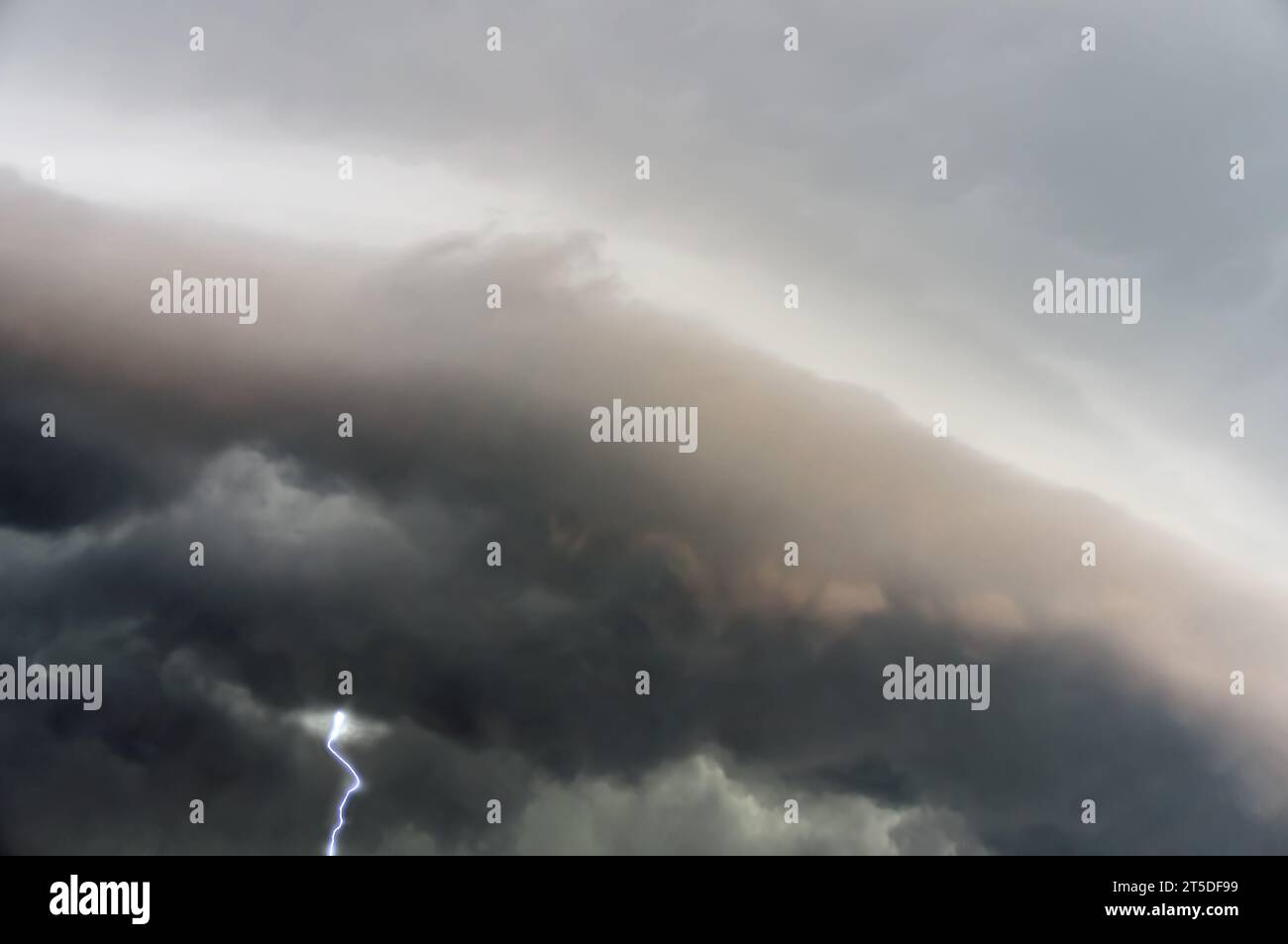 Looming dark storm clouds fill the sky, their ominous forms backlit by ...