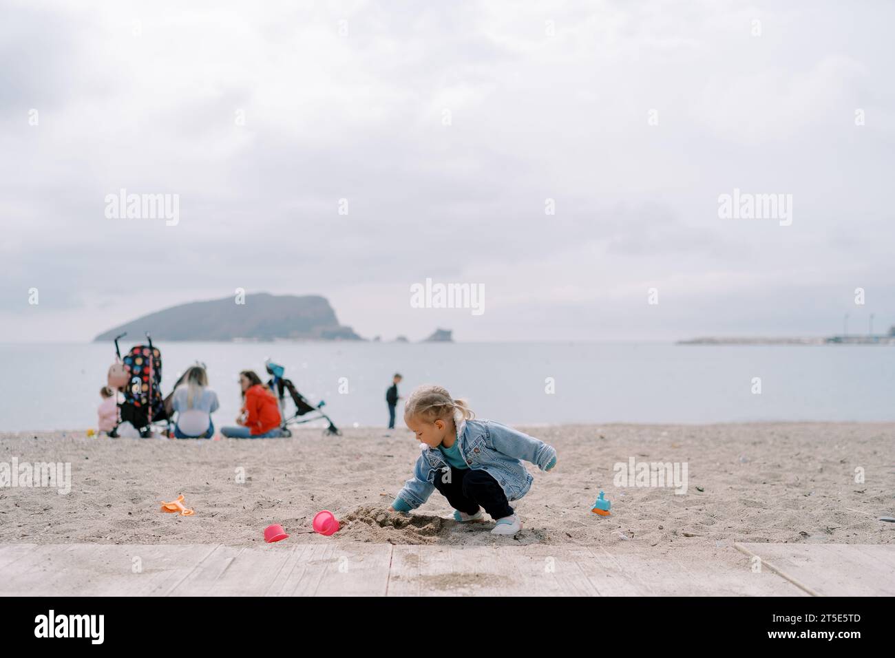 Little girl digs a hole in the sand while squatting against the ...