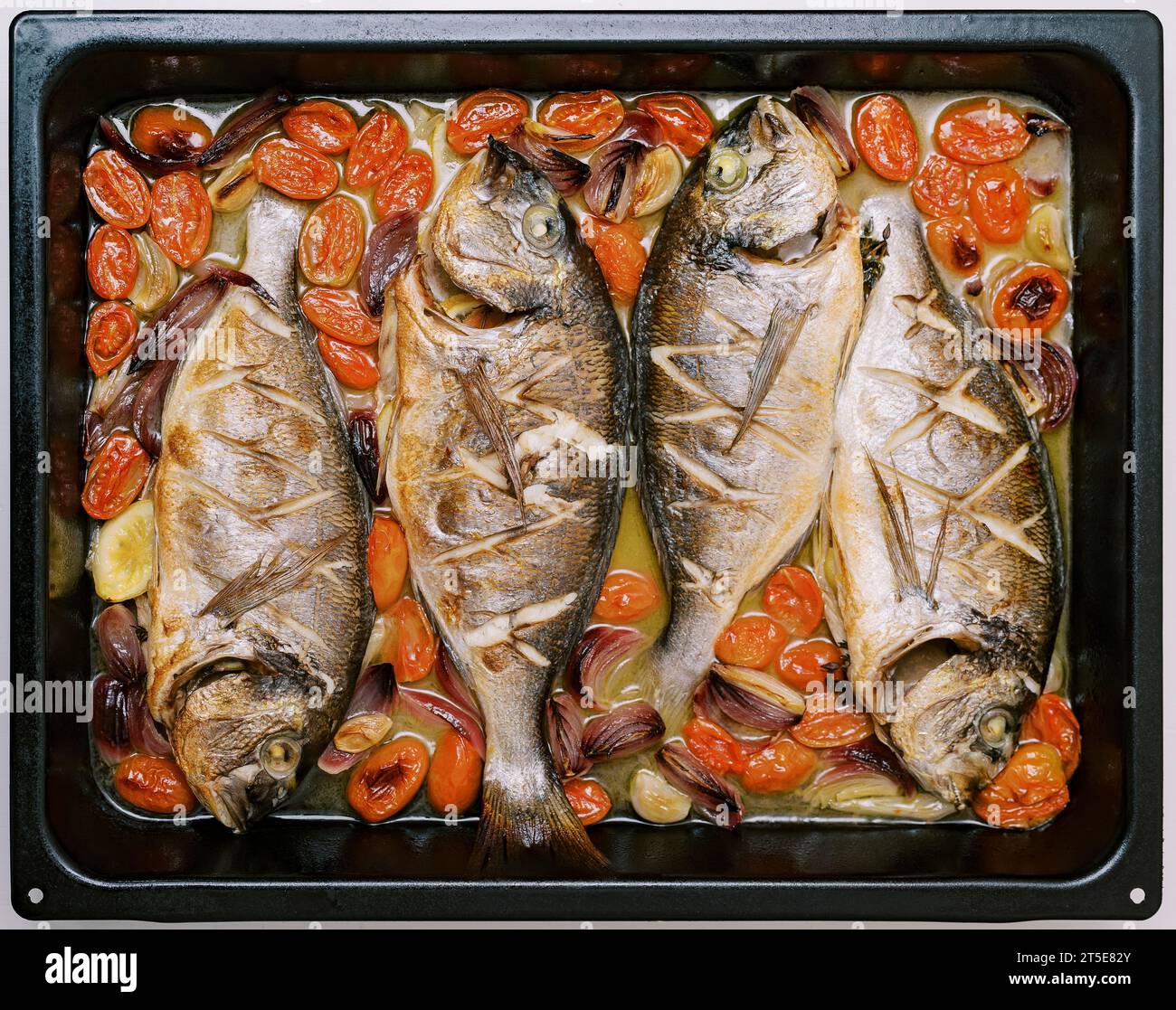Baked fish with chopped vegetables lies on a baking sheet. Top view ...