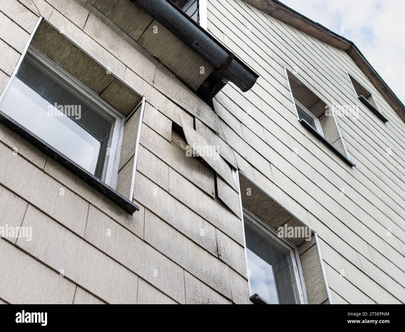 Broken asbestos sheets on a building facade. House cladding with toxic ...