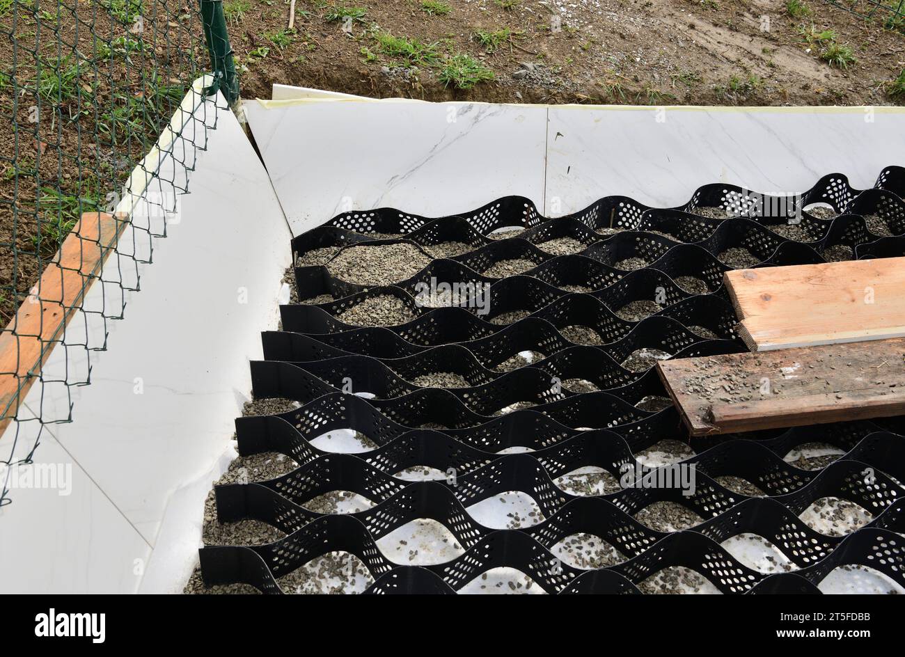 A bricklayer builds a parking for car using foil and crushed stone ...